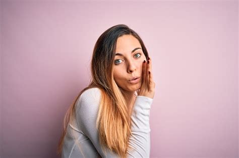 젊은 아름다운 금발의 여자 와 파란 눈 입고 흰색 티셔츠 위에 분홍색 배경 손 에 입 말하기 비밀 소문 속삭이는 악의적 인 대화 사생활에 대한 스톡 사진 및 기타 이미지