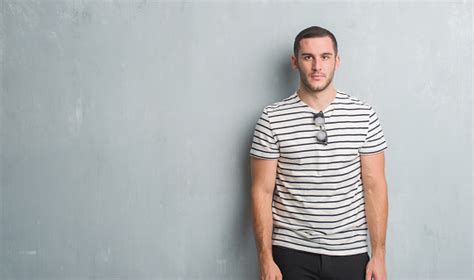 얼굴에 심각한 표정으로 회색 그런 지 벽에 젊은 백인 남자 간단 하 고 카메라를 보고 자연 T 셔츠에 대한 스톡 사진 및 기타