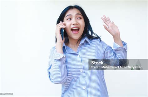 흰색 배경에 고립 된 줄무늬 셔츠를 입고 손바닥을 올리고 휴대 전화로 이야기하는 동안 놀란 행복한 아시아 여자 20 24세에
