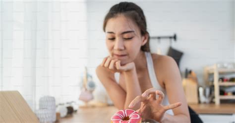 아시아의 아름다운 소녀는 배고프고 부엌에서 도넛을 먹고 싶어합니다 매력적인 여성은 운동 후 굶주린 느낌으로 스포츠 천을 입고 건강에 해로운 정크 푸드 음식 및 건강