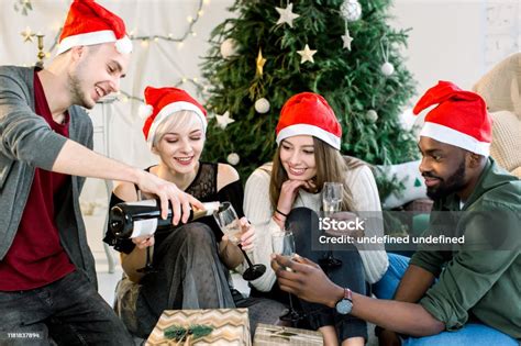 젊은 아프리카 남자와 백인 남자와 여자 20 받는 사람 30 세 산타 모자 와 함께 크리스마스 또는 크리스마스와 새해 축 하 파티에 대 한 샴페인을 마시는 안경을 Clink