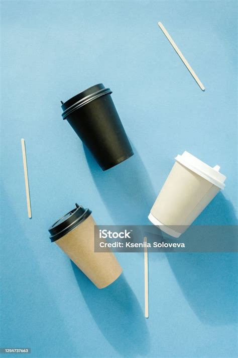 설탕을 혼합하기위한 커피와 나무 막대기를위한 세 가지 색종이 컵은 파란색 배경에 놓여 있습니다 하드 그림자커피 컵 테이크 아웃