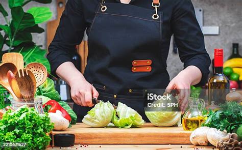 셰프가 빙산 양상추와 칼을 손에 들고 있습니다 나무 테이블 주방용품 야채 허브 요리 재료가 있는 아늑한 주방 건강한 비건 음식