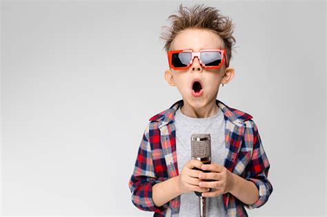 잘생긴 소년 격자 무늬 셔츠 회색 셔츠와 청바지에 회색 배경에 서 있다 선글라스를 착용 한 소년입니다 빨간 머리 소년 마이크에 노래 십대에 대한 스톡 사진 및 기타 이미지