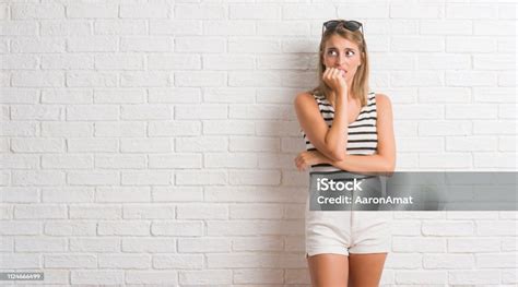 아름 다운 금발의 여 자가 젊은 찾고 스트레스와 긴장 하는 백색 벽돌 벽에 손톱을 물어 뜯고 입에 손 불안 문제입니다 백인종에 대한 스톡 사진 및 기타 이미지 Istock