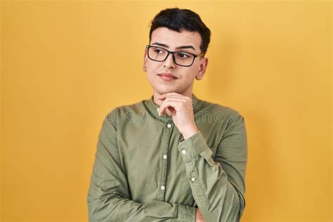 Non Binary Person Standing Over Yellow Background With Hand On Chin Thinking About Question