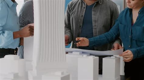 Close Up Of Workmates Analyzing Blueprints Plan And Building Model On Table Stock Footage