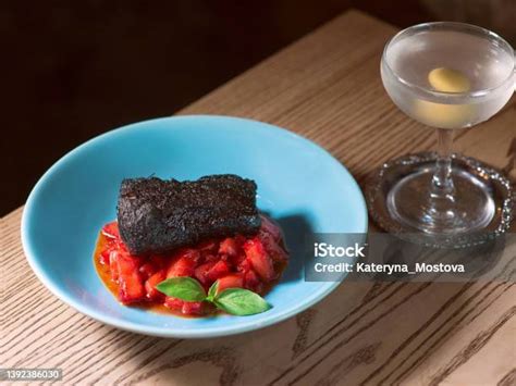 오징어 잉크에 절인 구운 돼지 고기 안심 파란 접시에 빨간 토마토와 바질 소금 후추 칼 붙이 및 드라이 버머스 알코올 칵테일과 올리브가 바의 테이블에 올려 놓은 0명에 대한