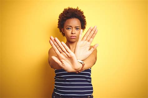 고립 된 노란색 배경 거부 표현 교차 팔과 손바닥을 통해 여름 티셔츠를 입고 Beauitul 아프리카 계 미국인 여성 부정적인 기호 화가 얼굴을하고 T 셔츠에 대한 스톡