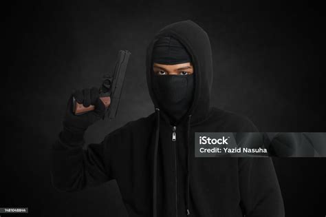 검은 후드티와 마스크를 쓰고 권총을 들고 총을 쏘는 수수께끼의 남자 어두운 주변 배경에 격리된 이미지 20 24세에 대한 스톡 사진 및 기타 이미지 Istock