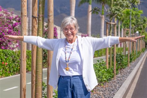 행복한 노인 여성은 균형을 유지하기 위해 팔을 뻗은 채 연석 위를 걷습니다 길에서 야외에서 장난기 많은 노인 은퇴자 70 79