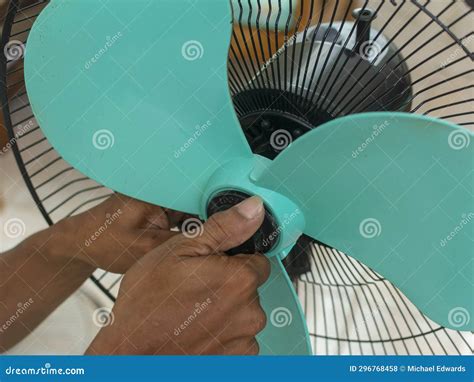 A Man Removes Or Unscrews The Fan Blade Lock Nut Of An Oscillating Electric Fan Cleaning And
