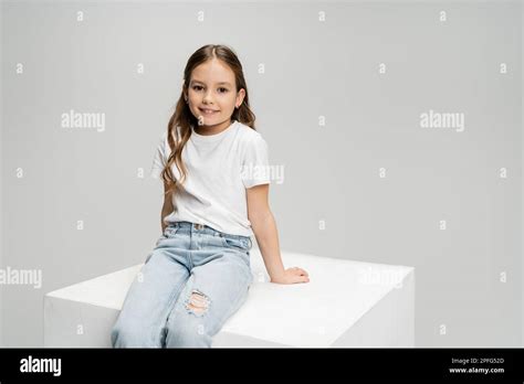 Smiling Preteen Girl In T Shirt And Jeans Sitting On Cube Isolated On