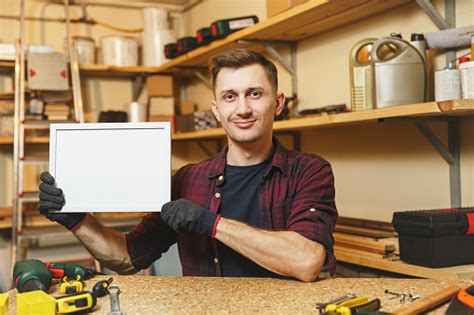 격자 무늬 셔츠에 잘생긴 백인 젊은 남자 장갑 나무 테이블에서 목공 워크숍에서 빈 프레임 다른 도구와 장소 텍스트에 대 한 빈 자리와 광고에 대 한 공간을 복사 합니다