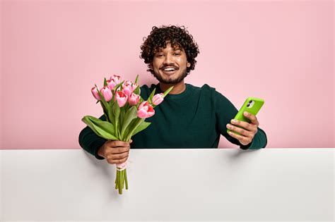 행복한 인도 남자가 스마트폰과 분홍색 배경에 튤립 무리를 들고 있다 기념일에 대한 스톡 사진 및 기타 이미지 기념일 꽃 식물 남성 Istock