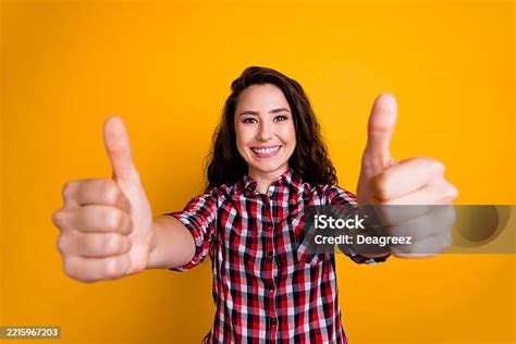 물결 모양의 머리를 한 이빨 빛나는 여자의 사진 체크 무늬 셔츠를 입고 엄지 손가락을 보여주는 노란색 배경에 고립 된 잘 했어