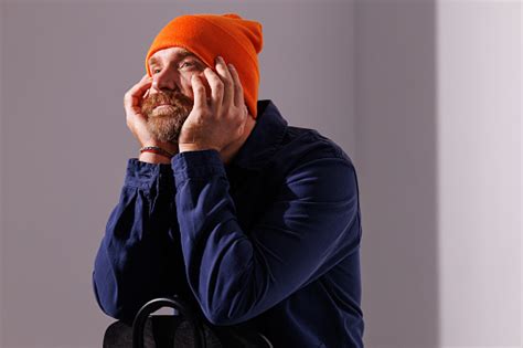 캐주얼 한 파란색 셔츠와 회색 배경에 의자에 앉아있는 Bight 모자를 쓴 세련된 수염 난 남자 40 44세에 대한 스톡 사진 및 기타 이미지 Istock