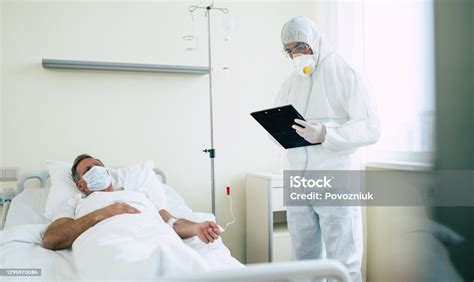 성인 남성 환자는 병원 병동에 있는 침대에 누워 있으며 보호복과 마스크를 착용한 의사의 검사를 받았습니다 2명에 대한 스톡 사진 및 기타 이미지 Istock