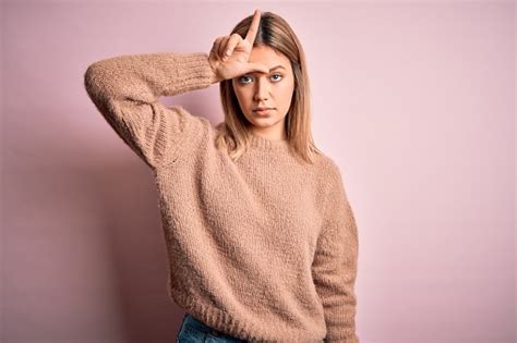 젊은 아름 다운 금발 여자 를 입고 겨울 울 스웨터 위에 분홍색 고립 된 배경 만드는 사람들 의 재미를 만드는 이마에 손가락으로 패자 제스처 조롱 하 고 모욕 겨울에 대한
