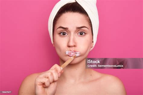 그녀의 머리에 어두운 머리와 흰색 수건을 가진 매력적인 백인 여성의 초상화 분홍색 스튜디오 벽에 고립 된 포즈 카메라를보고