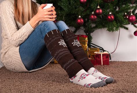 카펫 바닥에 앉아서 다리 백그라운드에서 커피와 따뜻하게 양말의 컵을 들고 젊은 여자는 크리스마스 트리와 선물 상자 가정 생활에 대한 스톡 사진 및 기타 이미지 Istock