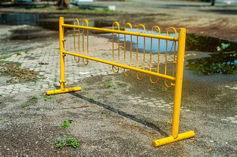 물웅덩이와 드문드문 풀이 있는 금이 가고 풍화된 포장 도로 위에 노란색 금속 바리케이드가 서 있는데 이는 유지 보수 중이거나 접근이 제한된 야외 구역임을 나타냅니다