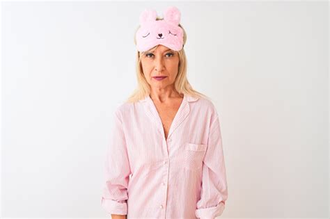 중년 여성은 수면 마스크와 잠옷을 입고 고립 된 흰색 배경 위에 얼굴에 심각한 표정으로 편안합니다 카메라를 보는 간단하고 자연스러운 노인에 대한 스톡 사진 및 기타 이미지