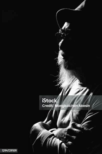 회색 수염과 콧수염을 입은 아시아 노인의 초상화는 검은 색과 흰색의 어두운 배경에서 포즈를 취하는 안경과 모자를 착용했습니다 60 69세에 대한 스톡 사진 및 기타 이미지