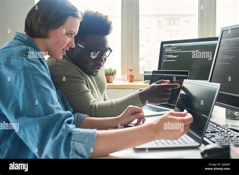 Female Programmer Pointing At Laptop With Software And Consulting With Colleague About Computer
