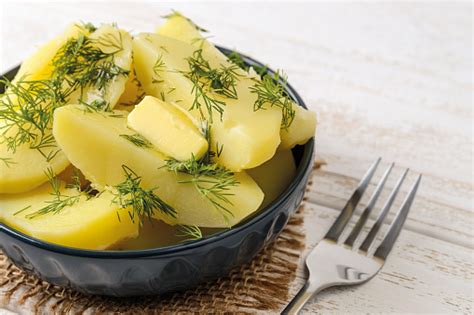 세라믹 그릇에 녹는 버터와 딜을 곁들인 갓 삶은 감자를 클로즈업하고 흰 나무 테이블에 포크를 넣습니다 집에서 맛있는 야채 요리를 요리하십시오 건강한 식생활 녹기에 대한 스톡