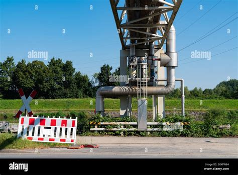 Red And White Barrier Near An Industrial Pipeline Crossing Made Of Metal And Supported By