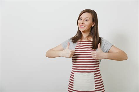 젊은 매력적인 웃는 갈색 머리 백인 주부 스트라이프 앞치마 흰색 배경에 고립에서 아름 다운가 정부 여자 엄지손가락 표시 카메라를 찾고 광고에 대 한 공간을 복사 합니다 가사