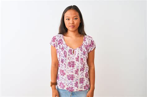 얼굴에 심각한 표정으로 고립 된 흰색 배경 위에 서있는 캐주얼 한 꽃 무늬 티셔츠를 입은 젊은 중국 여성 카메라를 보는 간단하고 자연스러운 T 셔츠에 대한 스톡 사진 및