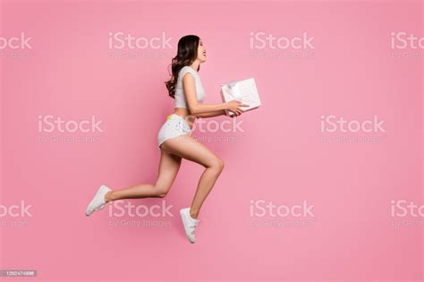 전체 길이 바디 사이즈 보기 프로필 측 좋은 매력적인 쾌활 한 쾌활 한 물결 모양의 여자 점프 실행 잡고 손 선물 상자 배달 고립 된 핑크 파스텔 색상 배경 반바지에 대한