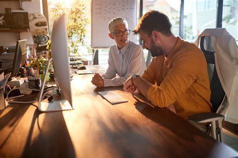 한 연로한 사업가가 사무실 책상에서 일하는 동안 젊은 남성 동료와 대화를 나누고 있습니다 비즈니스 사무실 직업 20 29세에 대한 스톡 사진 및 기타 이미지 Istock