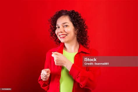 곱슬 귀여운 소녀가 웃고 춤을 춘다 밝은 빨간색 배경에 젊은 여자의 스튜디오 초상화 밝은 옷을 입은 긍정적 인 예쁜 여성 공간을