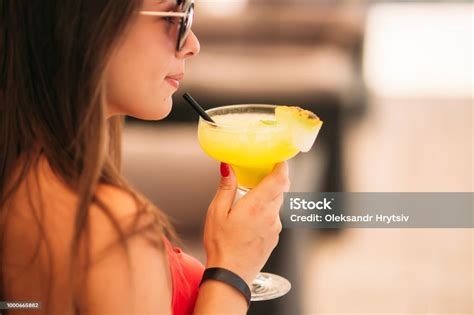 비치 클럽 바의 오두막에 앉아 화려한 칵테일을 마시는 수영복을 입고 아름 다운 젊은 여자 여름 시간에 그녀의 음료를 즐기는 멋진