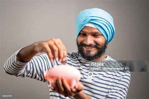 젊은 인도 시크교 남자는 회색 배경에 돼지 저금통에 동전을 배치하여 돈을 절약 저축과 미래의 재정 계획 및 투자의 개념 계획에 대한 스톡 사진 및 기타 이미지 Istock