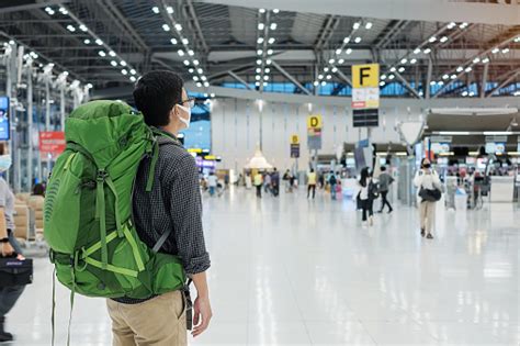 젊은 남자 여행자 의료 얼굴 마스크를 착용 하 고 공항 터미널에서 비행 시간을 확인 보호 코로나 바이러스 질병 감염 새로운 노멀