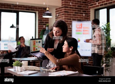 Diverse Team Of Women Analyzing Report On Laptop In Disability Friendly Office Working With