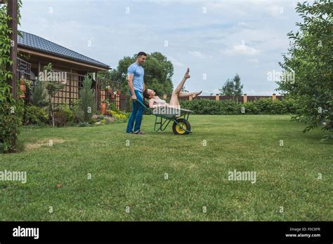 Full Length Of Man Pushing Girlfriend In Wheelbarrow At Backyard Stock Photo Alamy
