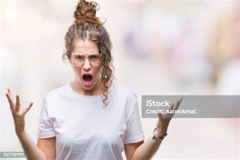 아름 다운 젊은 갈색 머리 곱슬 머리 소녀는 고립 된 배경 위에 안경을 쓰고 미친 소리와 공격적인 표현과 팔이 제기 소리 좌절