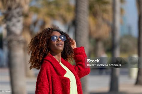 화창한 날에 웃 고 머리를 만지고 있는 동안 거리 도시에서 선글라스와 빨간 자 켓 서 입고 젊은 아름 다운 곱슬 아프리카 여자의 전면 보기 곱슬 머리에 대한 스톡 사진 및