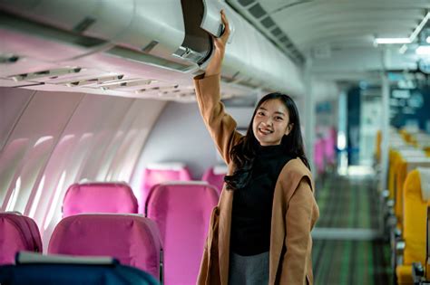 비행기 탑승 시 머리 위 선반에 기내 반입 가방을 보관하는 여성 여행자는 다가오는 여행에 대한 즐거운 기대감을 표현합니다 20 29세에 대한 스톡 사진 및 기타 이미지