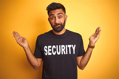 고립 된 노란색 배경 단서와 팔과 손을 들고 혼란 스러운 표정 위에 보안 유니폼을 입고 아랍 인도 히스패닉 보호 남자 의심 개념 감시에 대한 스톡 사진 및 기타 이미지
