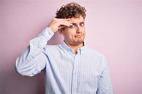 젊은 금발 잘생긴 남자 와 곱슬 머리 입고 줄무늬 셔츠 위에 흰색 배경 걱정 하 고 이마에 손에 문제에 대 한 스트레스 긴장과 위기에 대 한 불안 개념에 대한 스톡 사진 및