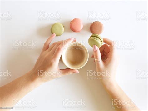 여자 손은 위에서 흰색 테이블에 커피 한 잔 케이크 마카롱을 들고있다 여성 근무 데스크 아늑한 아침 식사 여성의 손에 맛있는 커피와 다채로운 마카롱의 화이트 컵 손에 대한