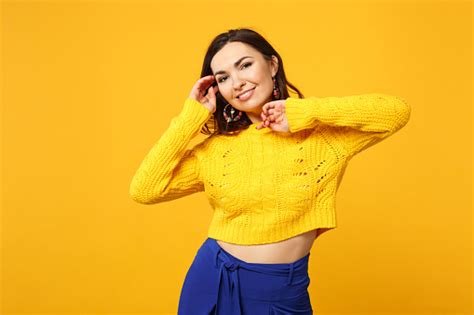 스웨터에 즐거운 젊은 여자의 초상화 파란색 바지 카메라를 찾고 노란 오렌지 배경에 고립 된 얼굴 가까이 손을 유지 사람들은 진심으로 감정 라이프 스타일 개념입니다 복사