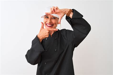 유니폼과 모자를 입고 고립 된 흰색 배경 위에 서있는 중년 요리사 여성은 행복한 얼굴로 손과 손가락으로 프레임을 만드는 미소 창의력과 사진 개념 손가락에 대한 스톡 사진 및