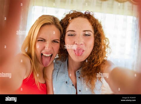 Portrait Of Two Female Friends Sticking Out Tongues While Looking At